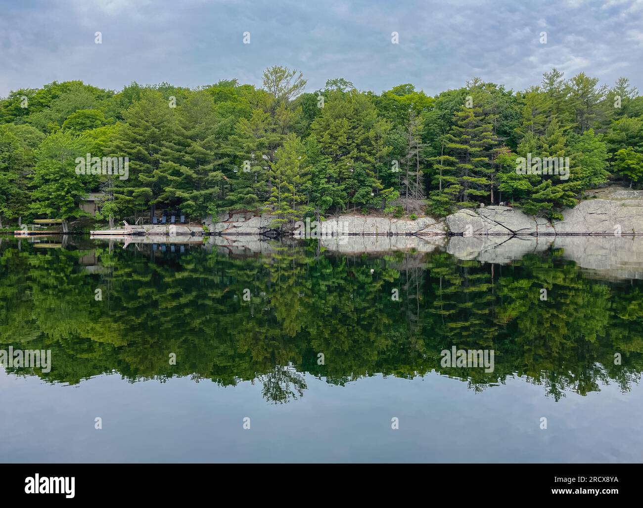 Shoreline view of still lake with clear reflection of rocks and trees ...