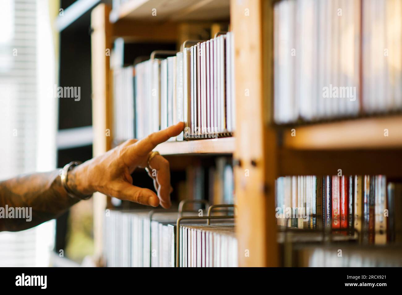 man searching through cds on a bookshelf with his hand Stock Photo - Alamy
