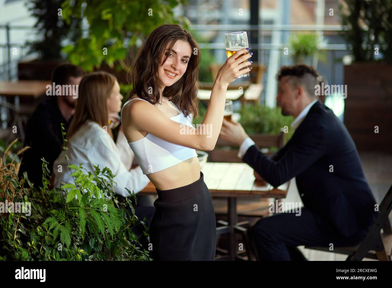 Focus on beautiful smiling girl raising beer glass. Blurred people on ...