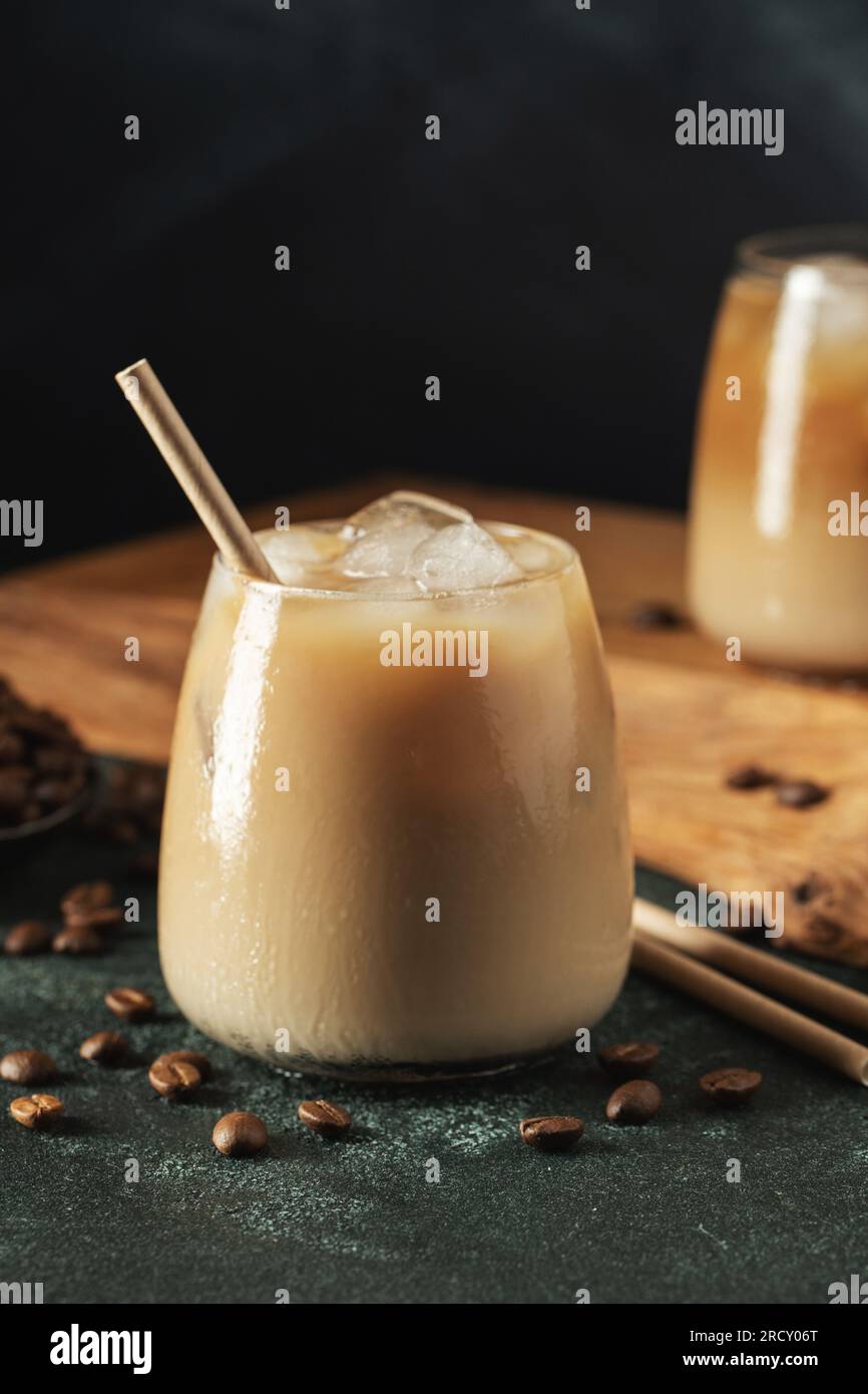 Ice coffee in a tall glass with cream poured over, ice cubes and beans ...
