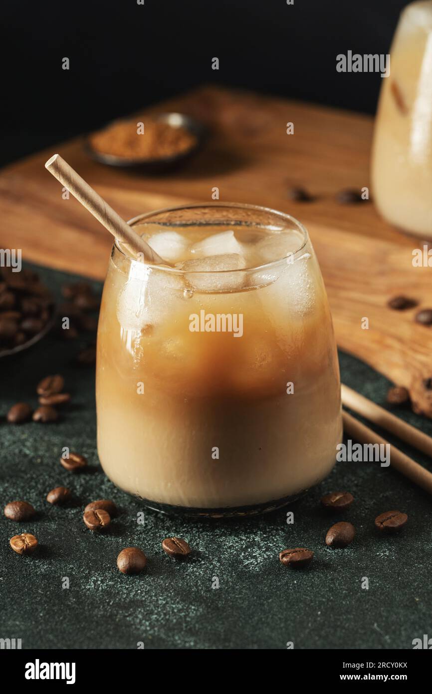 Ice coffee in a tall glass with cream poured over, ice cubes and beans ...