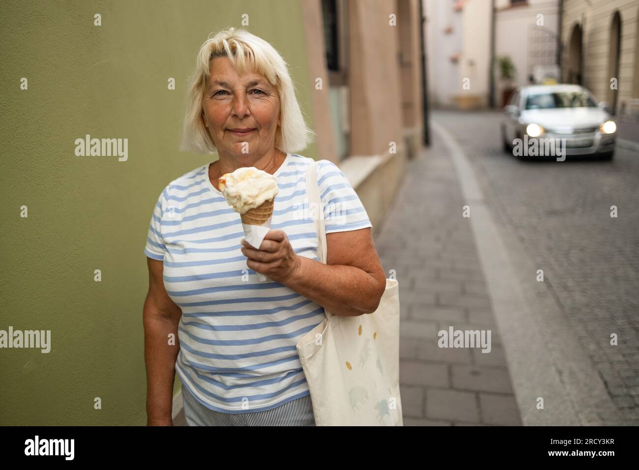 Happy 60s woman with delicious ice cream in waffle cone outdoors. Space ...