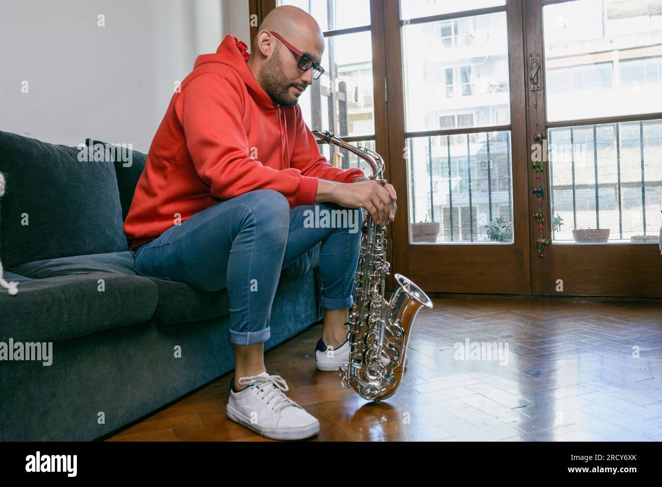 young latin musician man at home sitting on the sofa calm looking down ...