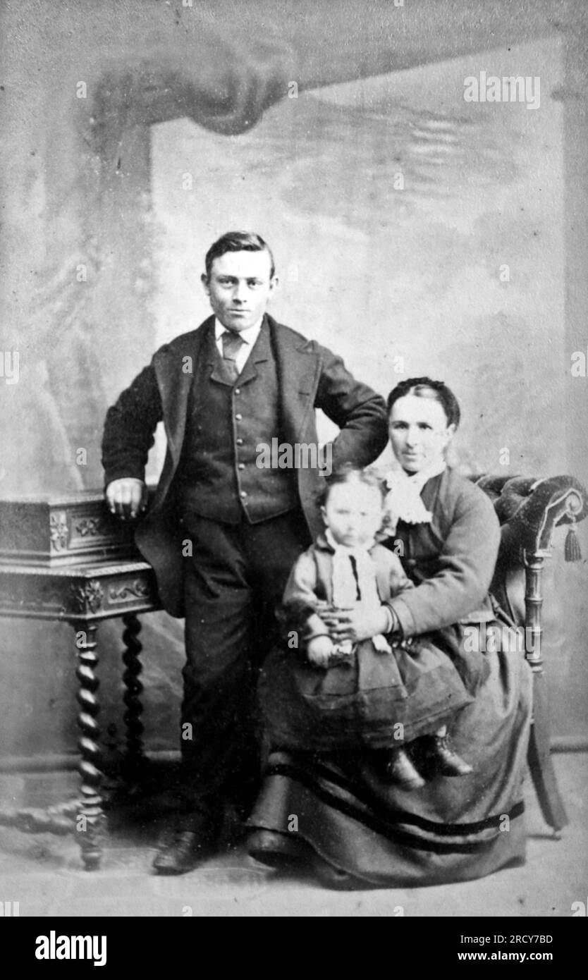 Portrait of a man standing beside a lady with a child on her lap ...