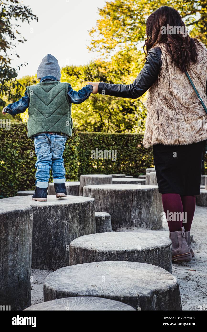 Mother helping her son move his first steps. Mom hand in hand with her ...