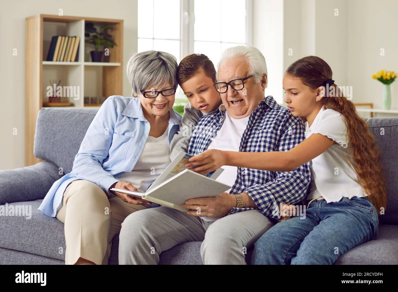 Grandparents reading a book to their grandchildren sitting at sofa at ...