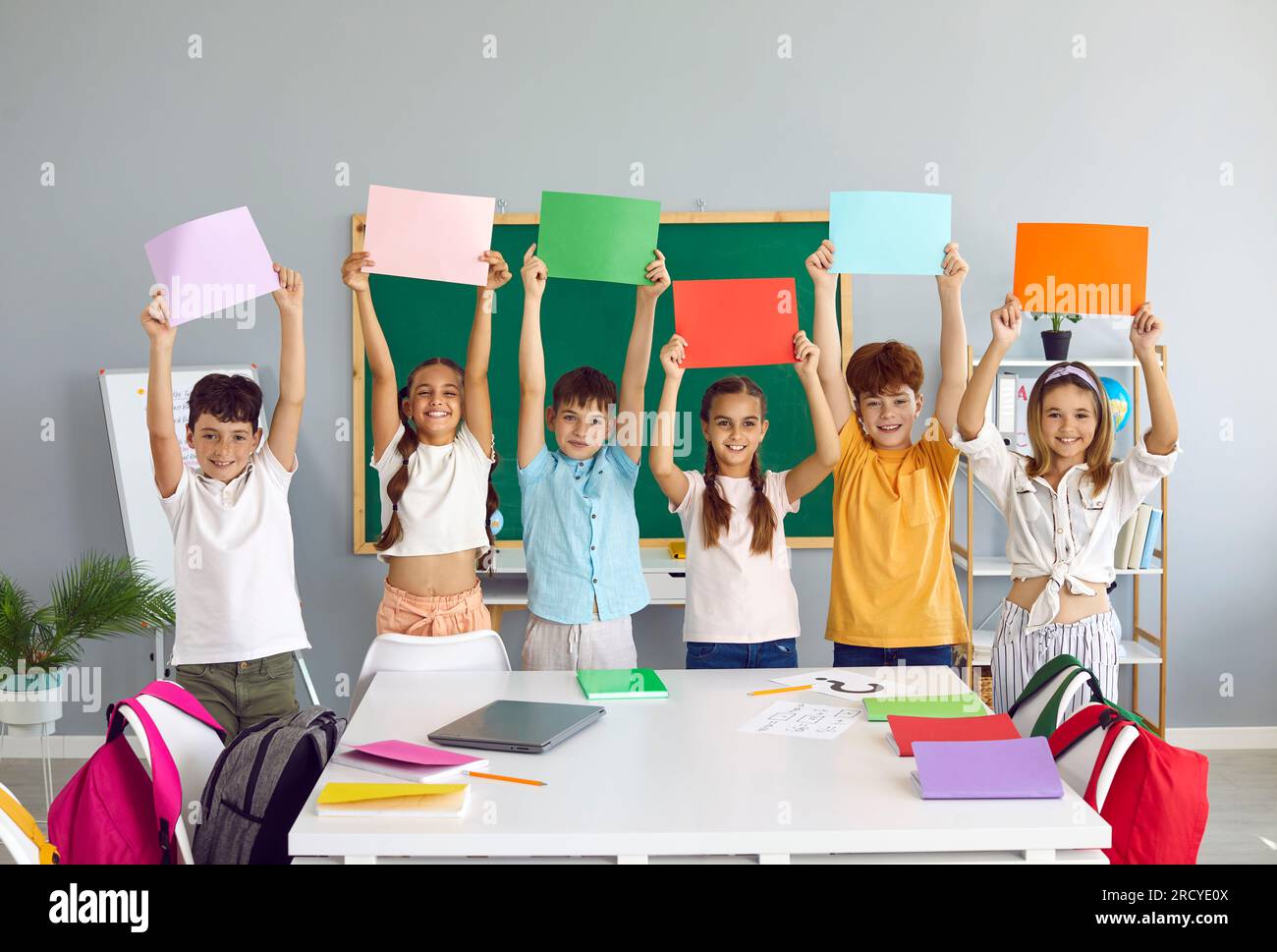 Happy elementary school students standing in classroom and holding ...