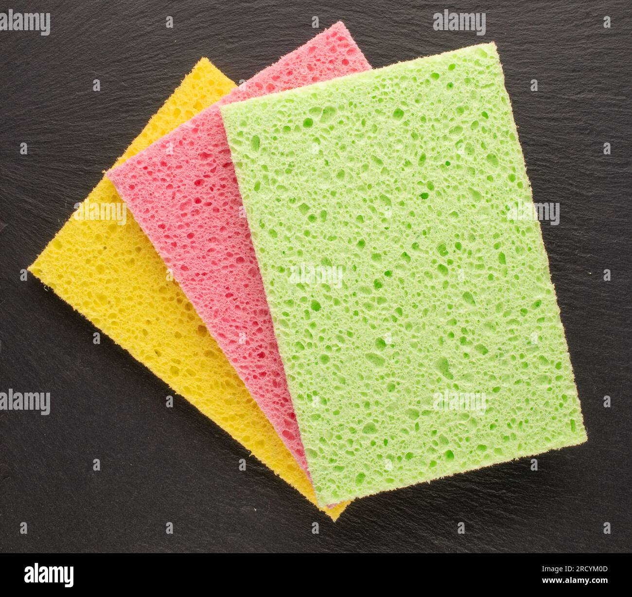 Three colored cellulose kitchen sponges on slate stone, macro, top view ...