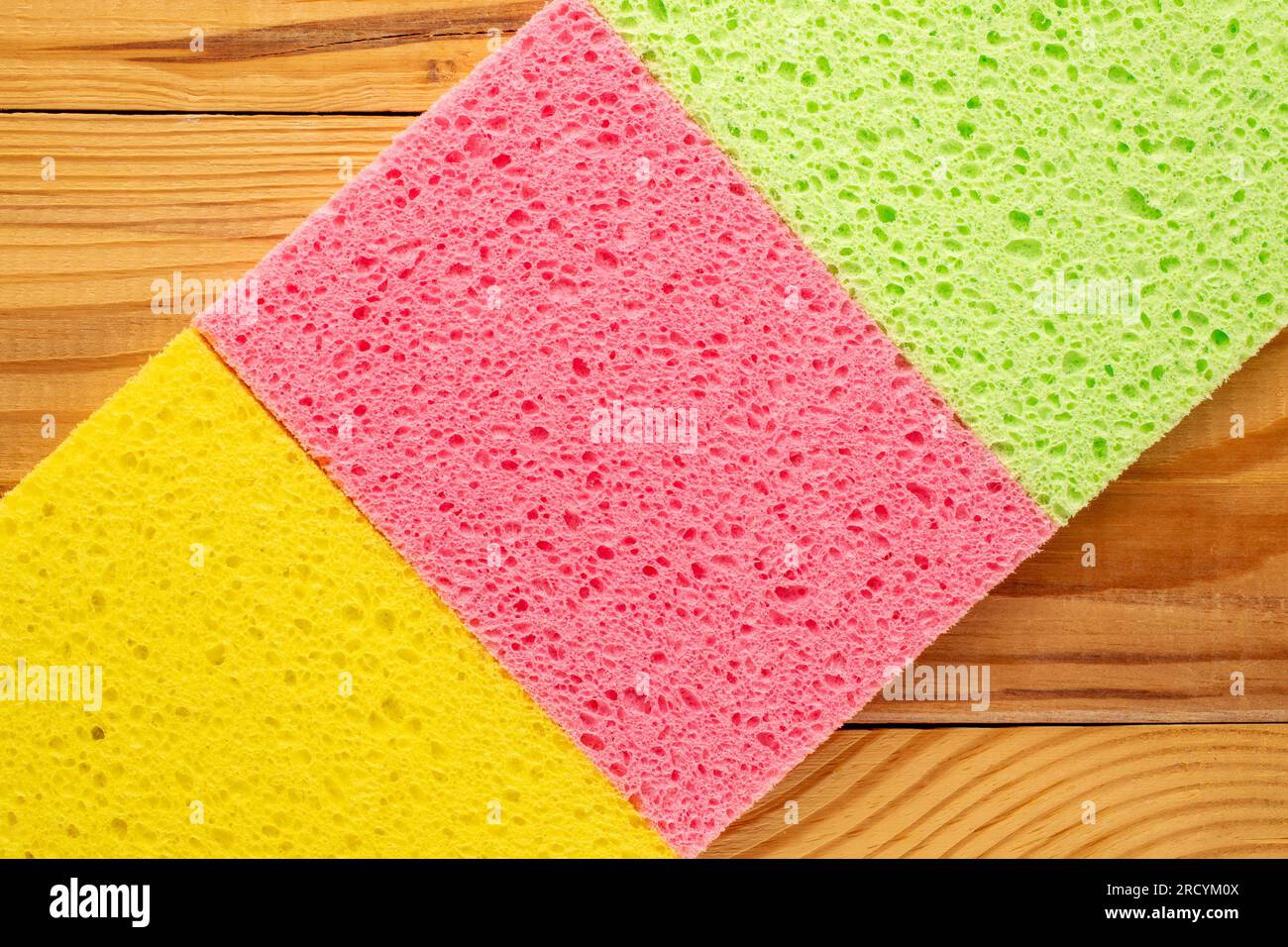 Three colored cellulose kitchen sponges on a wooden table, macro, top ...