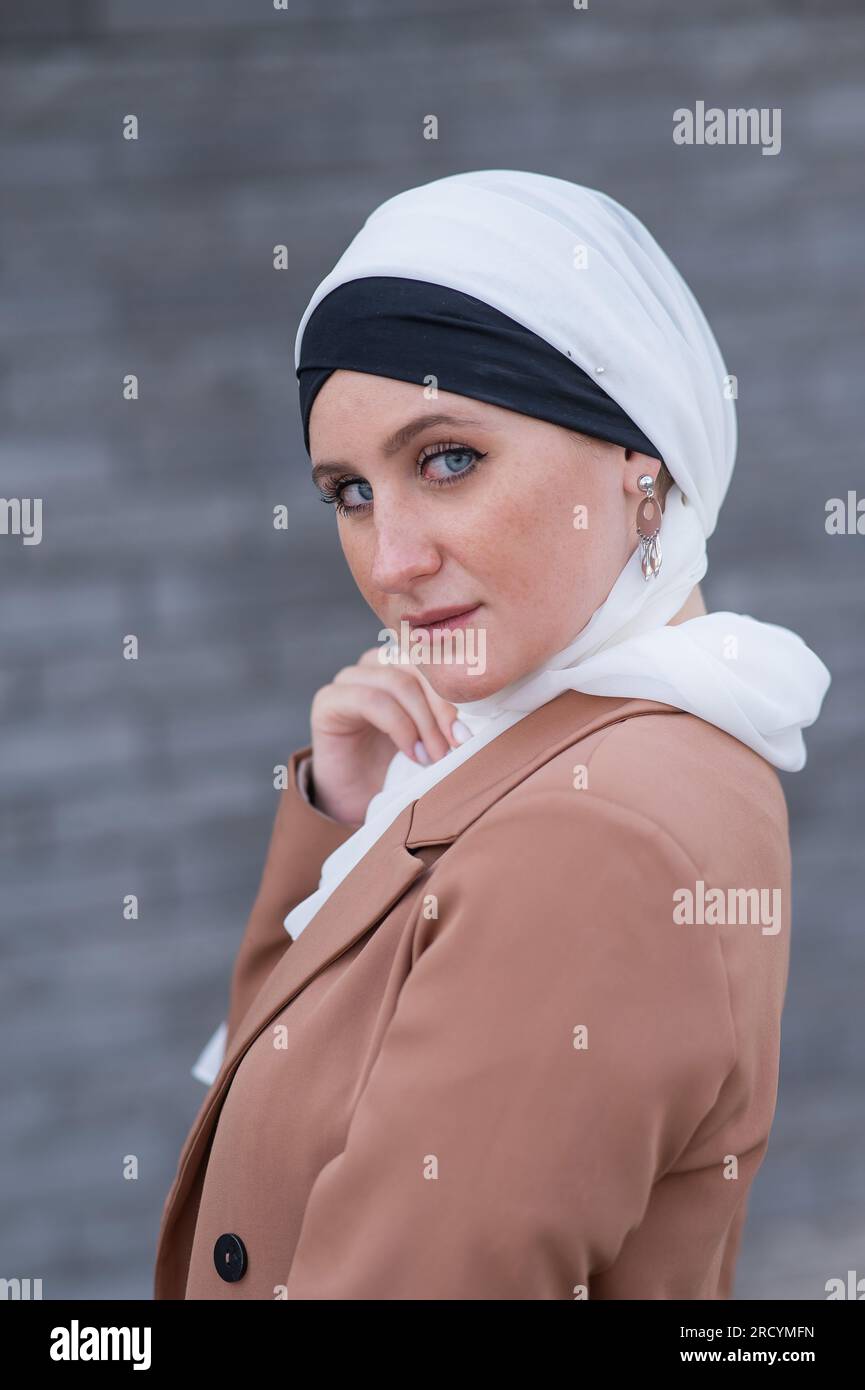 Portrait of a young blue-eyed woman in a hijab against a gray brick ...