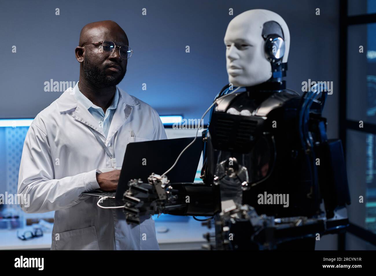 African American engineer in lab coat using laptop to control the robot ...