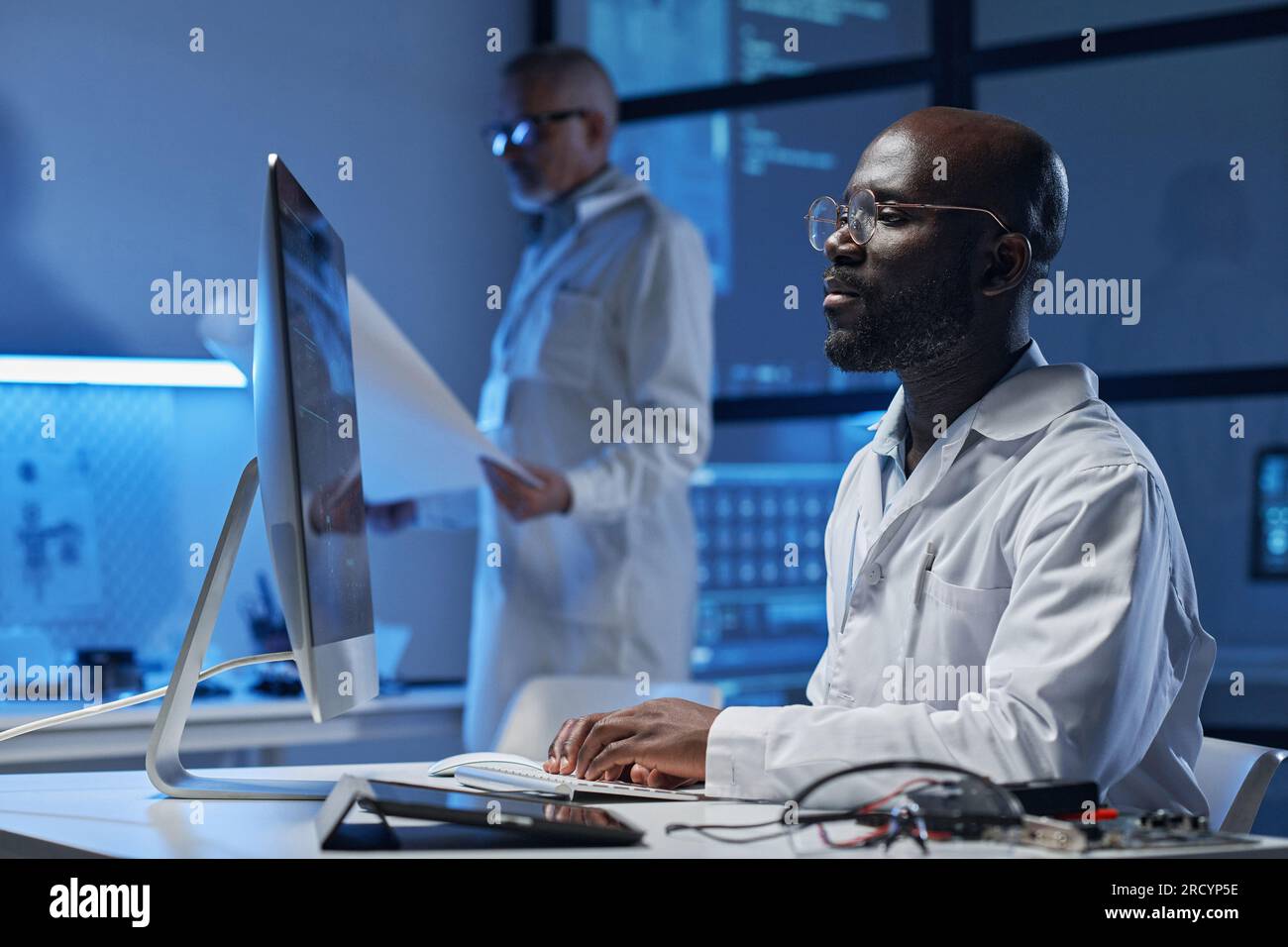 African American engineer sitting at table in front of monitor and ...