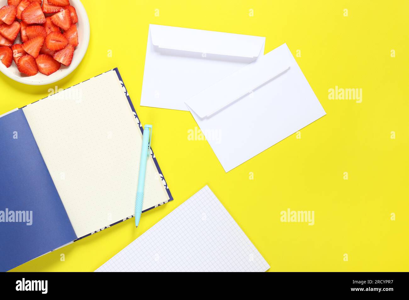 An open notepad, letter envelopes, a pen and a plate with strawberries ...