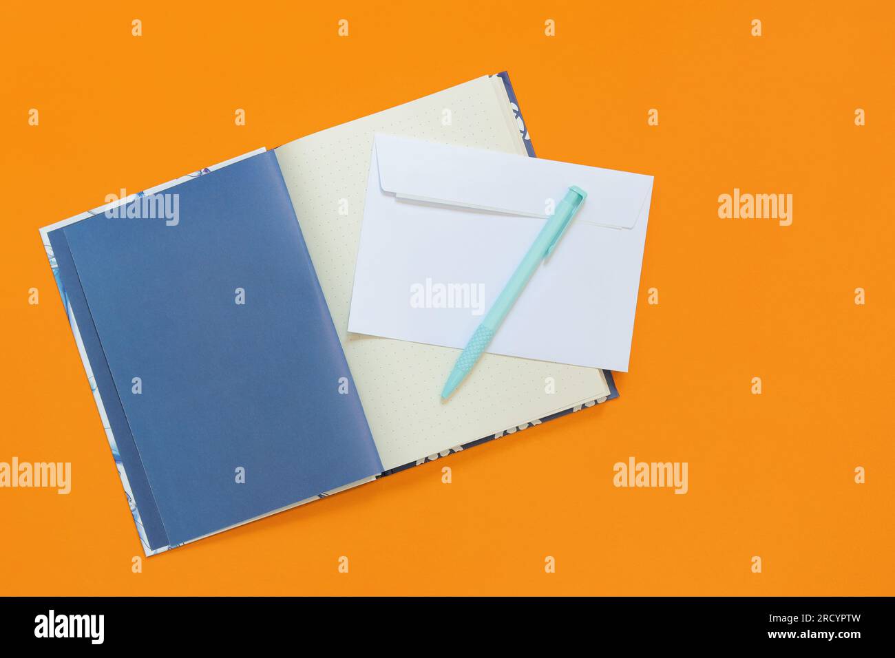 An open diary for notes, a white envelope and a pen on a bright orange ...
