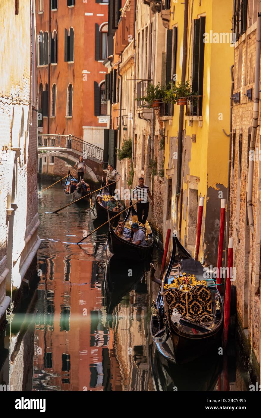 Touristic gondola in narrow grand canal between buildings in Venice, Italy. On boat is a ...