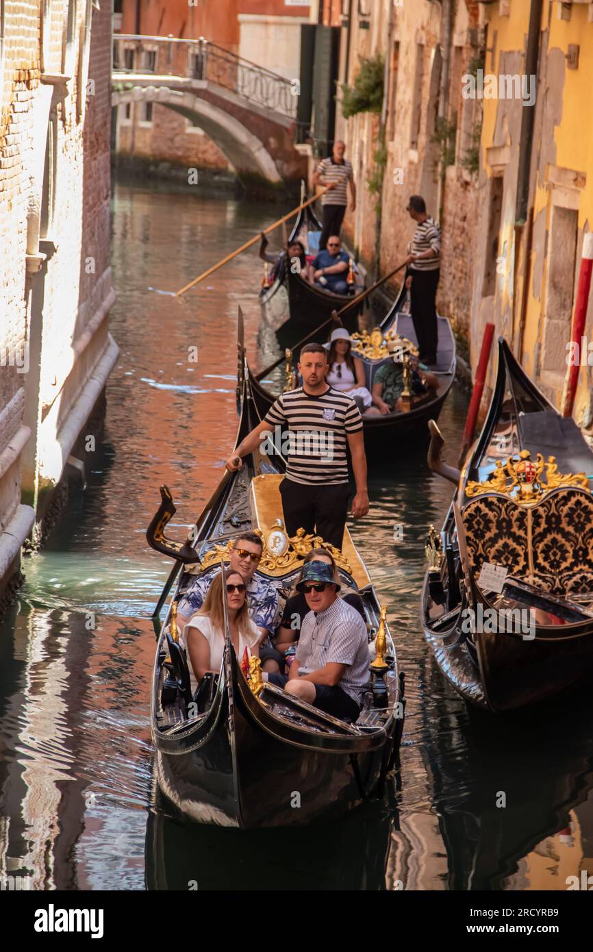 Touristic gondola in narrow grand canal between buildings in Venice, Italy. On boat is a ...