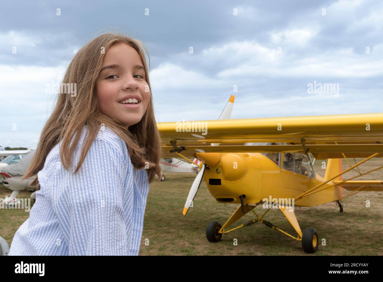 Smiling teenage girl in front of a vintage yellow plane on the airfield ...