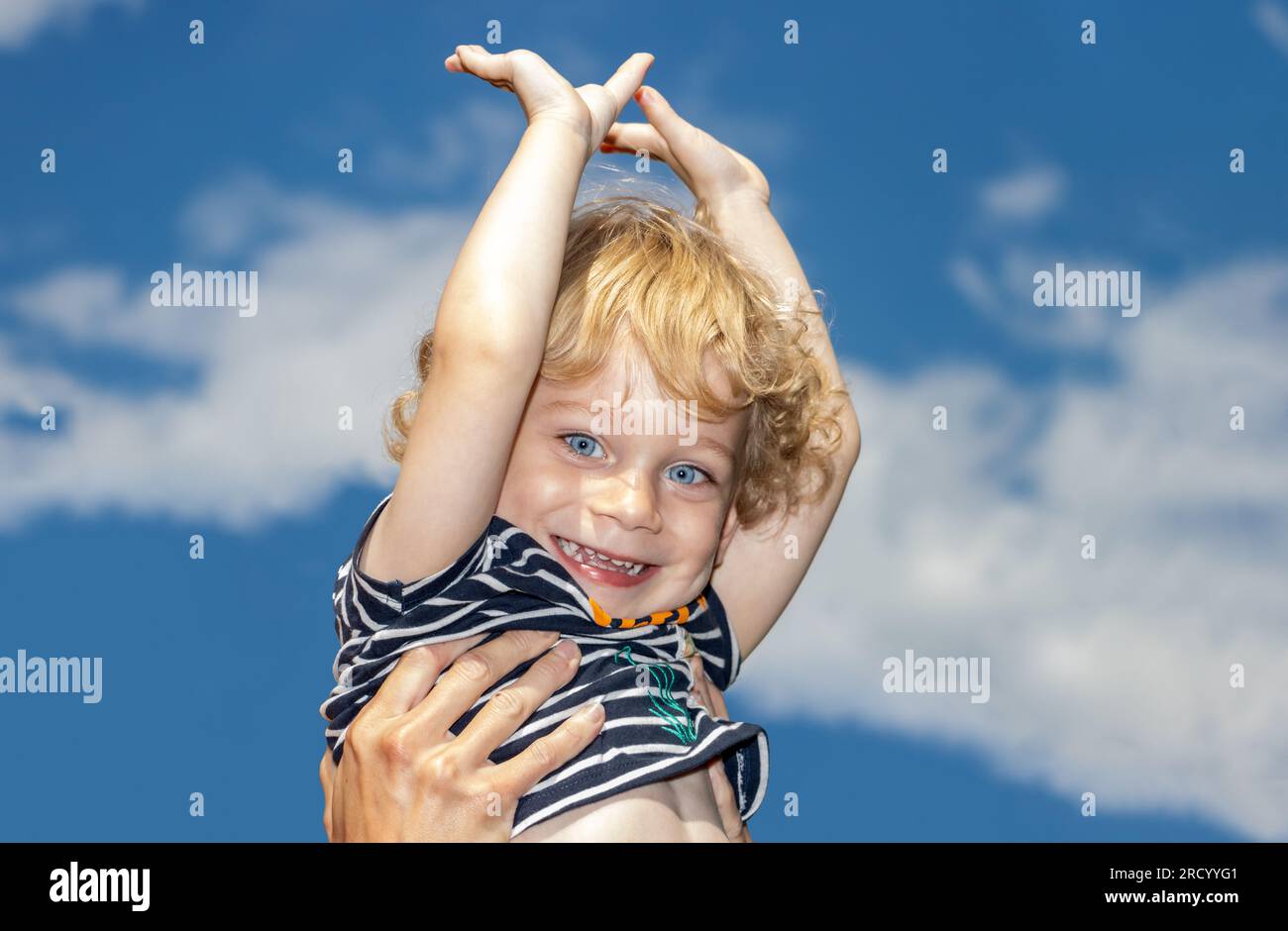 A cheerful boy is lifted up against the background of a summer sky ...