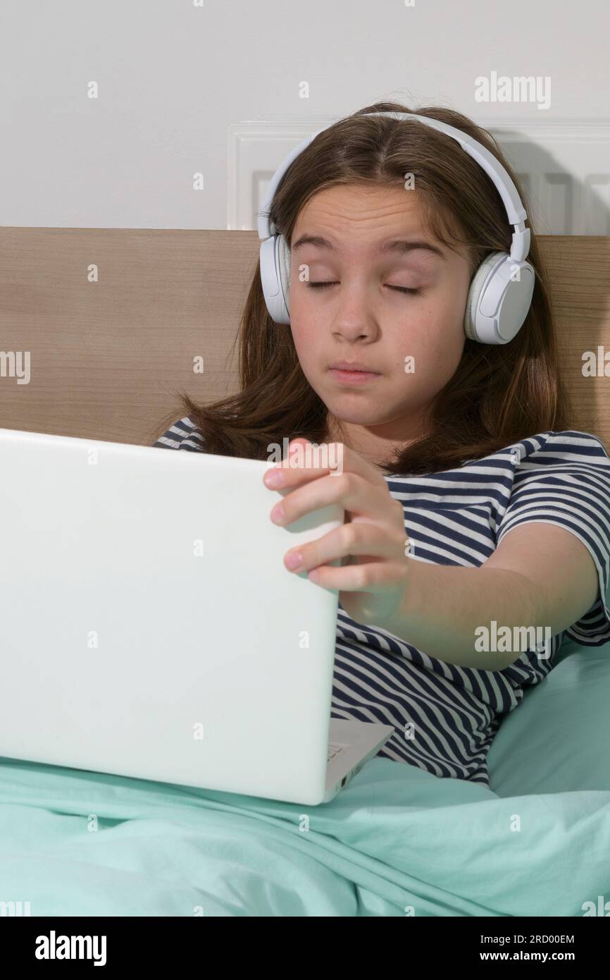 Tired in bed of the computer, the teen girl is going to sleep. vertical ...