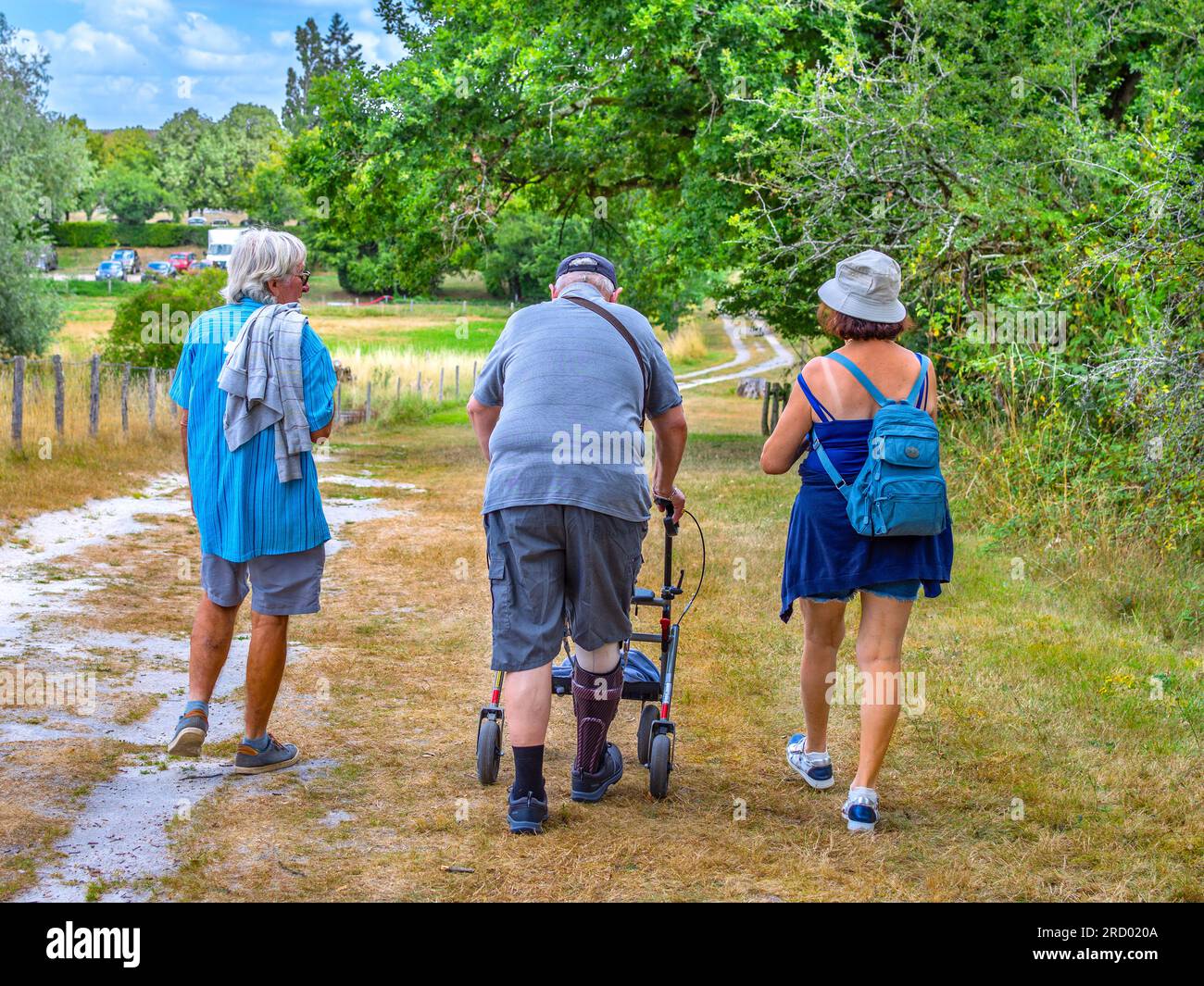 Three people walking along country track, one man with walking frame ...