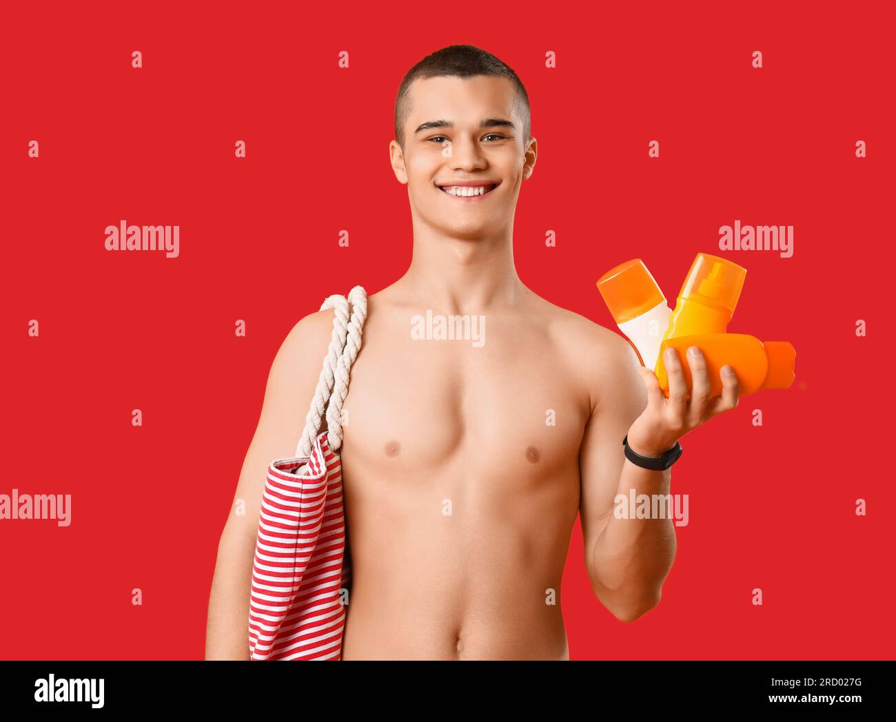 Teenage boy with bottles of sunscreen cream on red background Stock ...