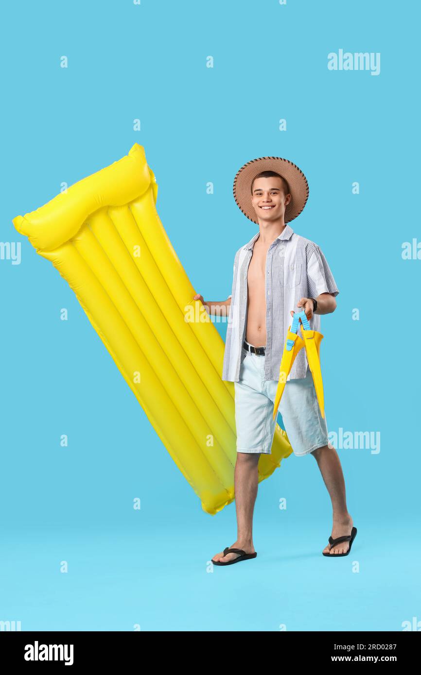 Teenage boy with inflatable mattress and flippers on blue background ...