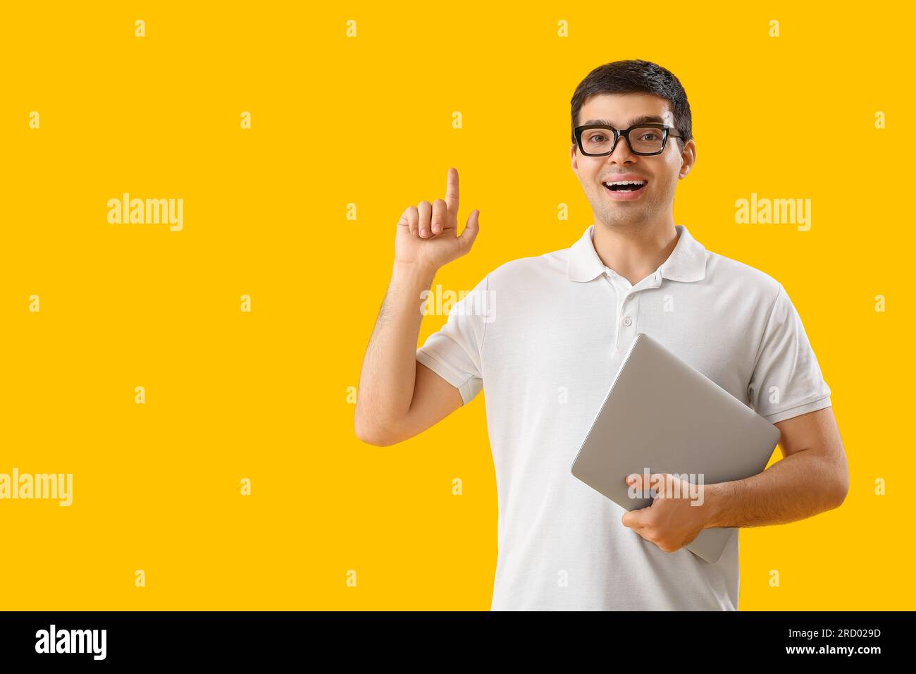 Male programmer with laptop pointing at something on yellow background ...