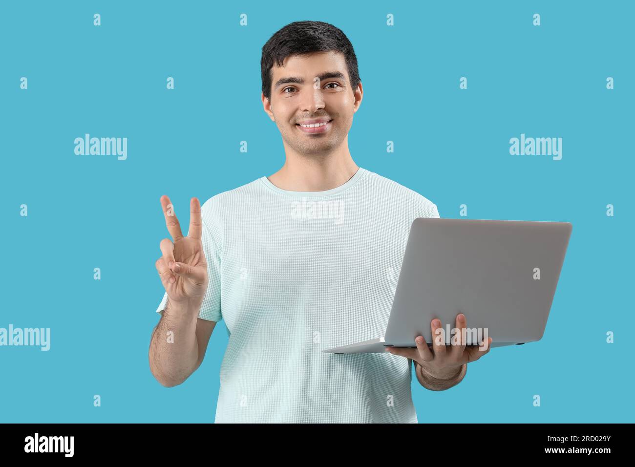 Male programmer with laptop showing victory gesture on blue background Stock Photo - Alamy