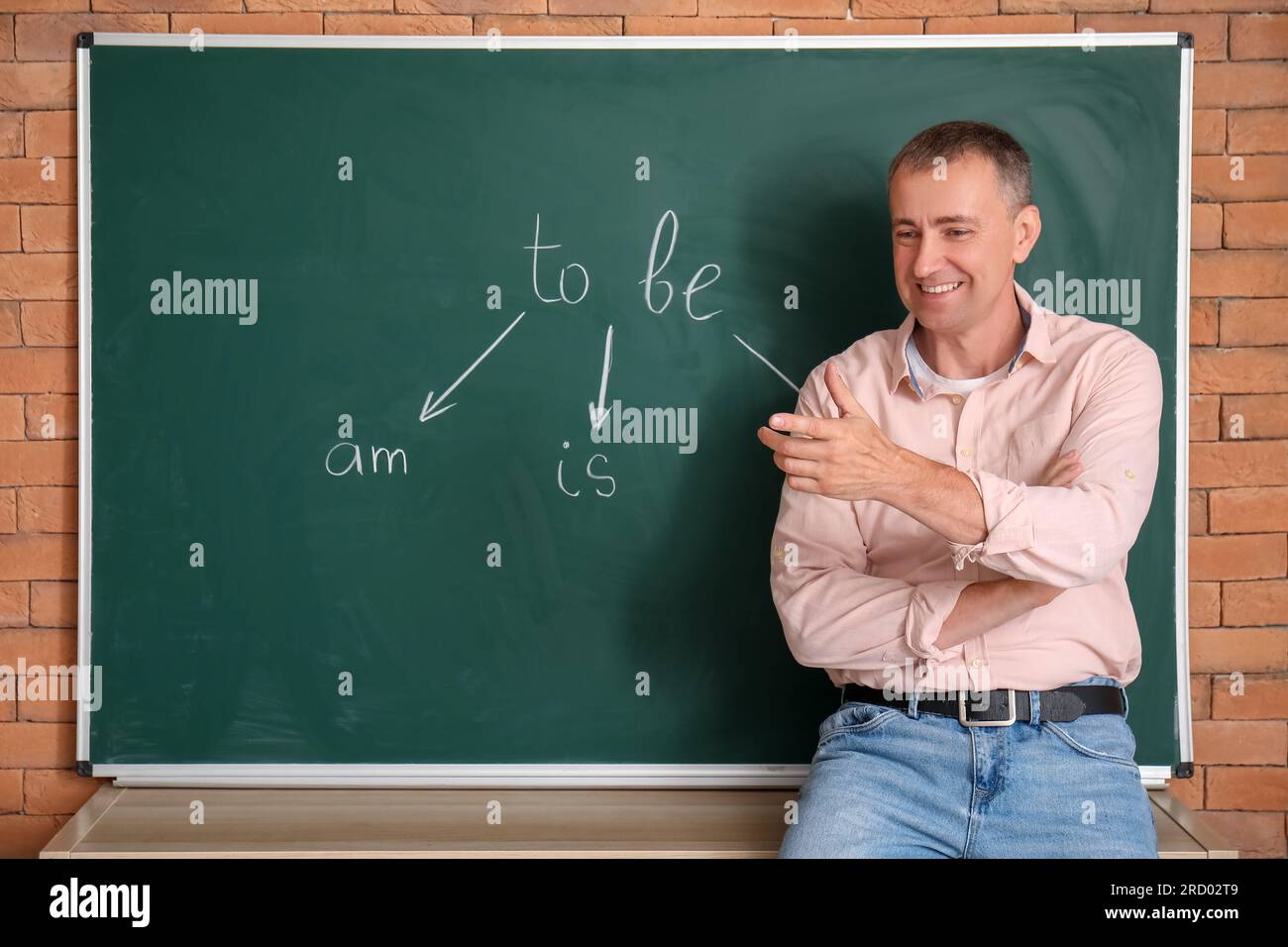 Male teacher conducting English grammar lesson near blackboard in ...