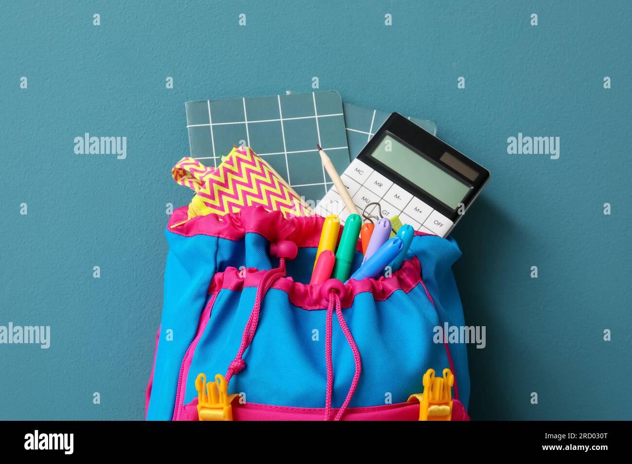 Colorful backpack with different stationery and calculator on blue ...
