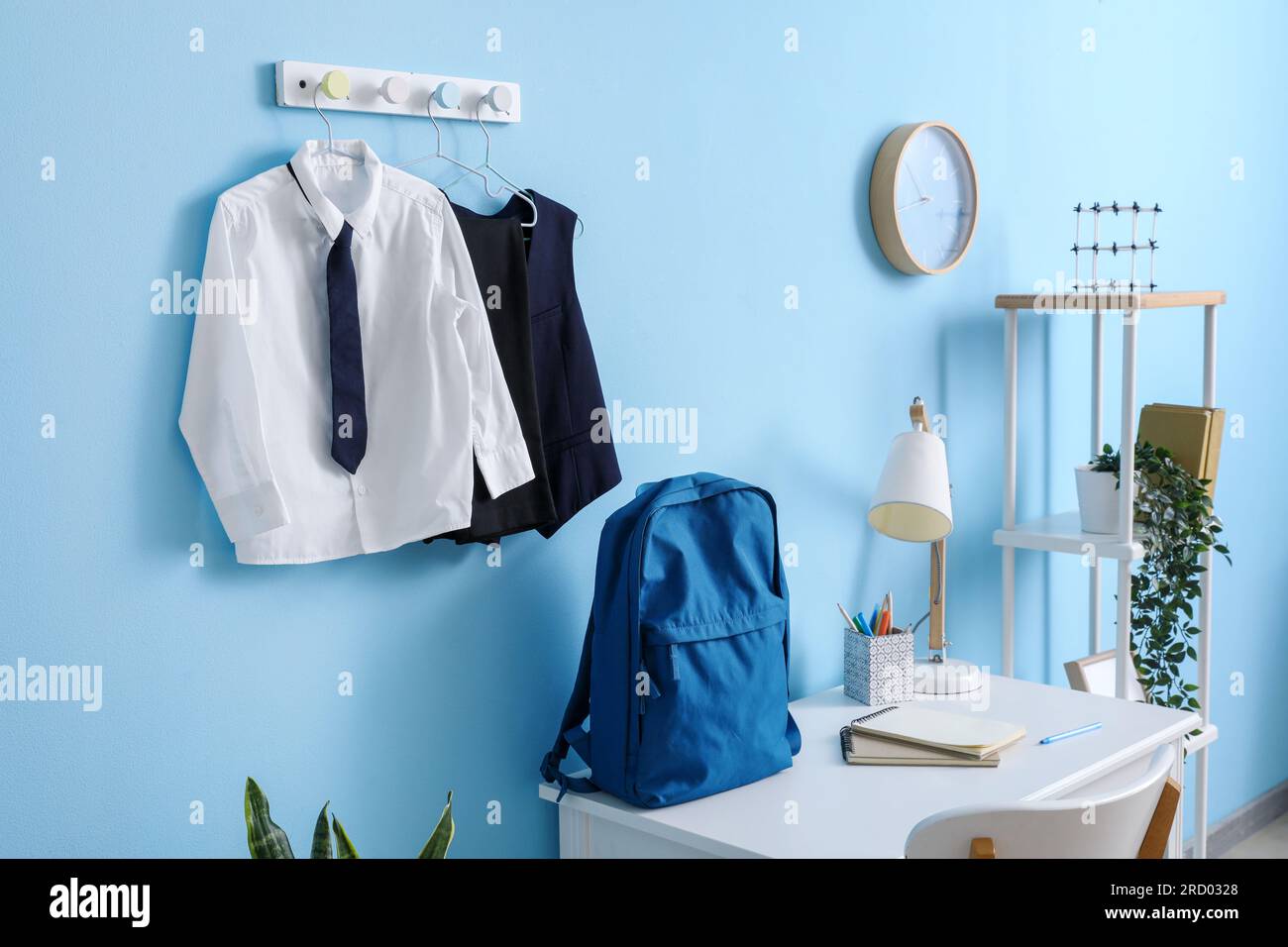 Desk with backpack and stylish school uniform hanging on blue wall in ...