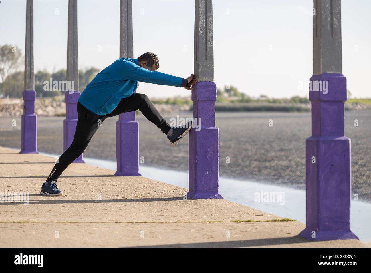 Latino runner stretching against a column of a pergola in a public park ...