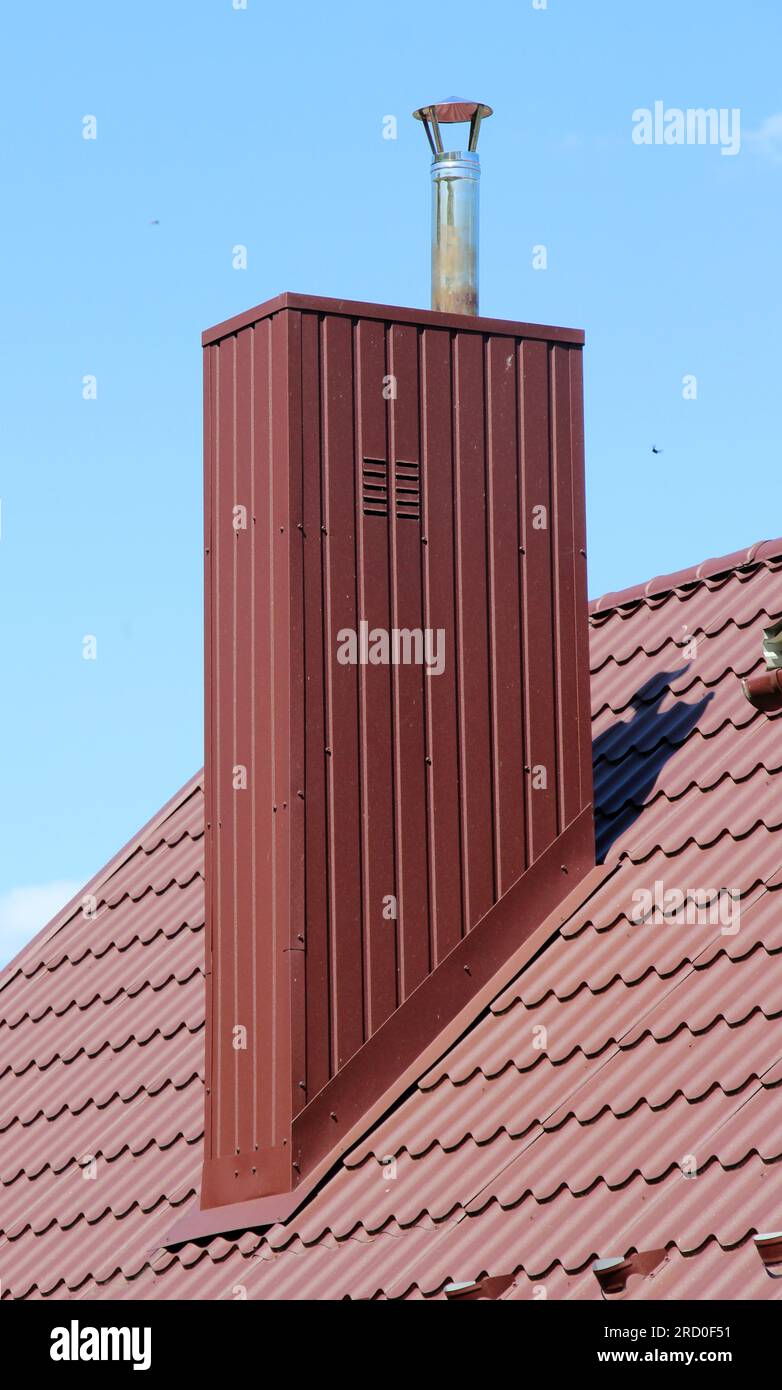 A chimney on the roof of a house covered with metal tiles or a metal ...