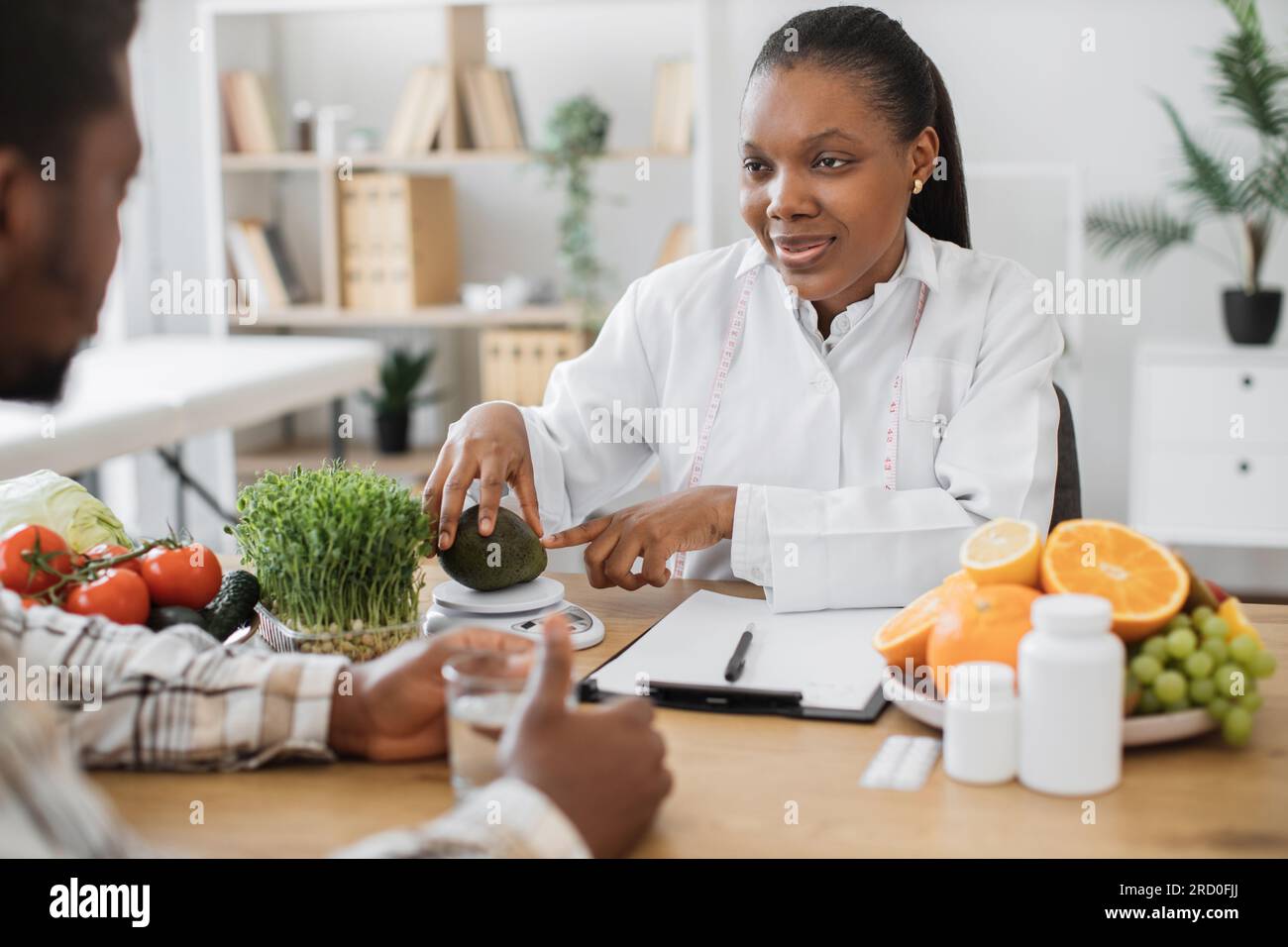 African american dietitian in white coat putting fresh avocado on ...