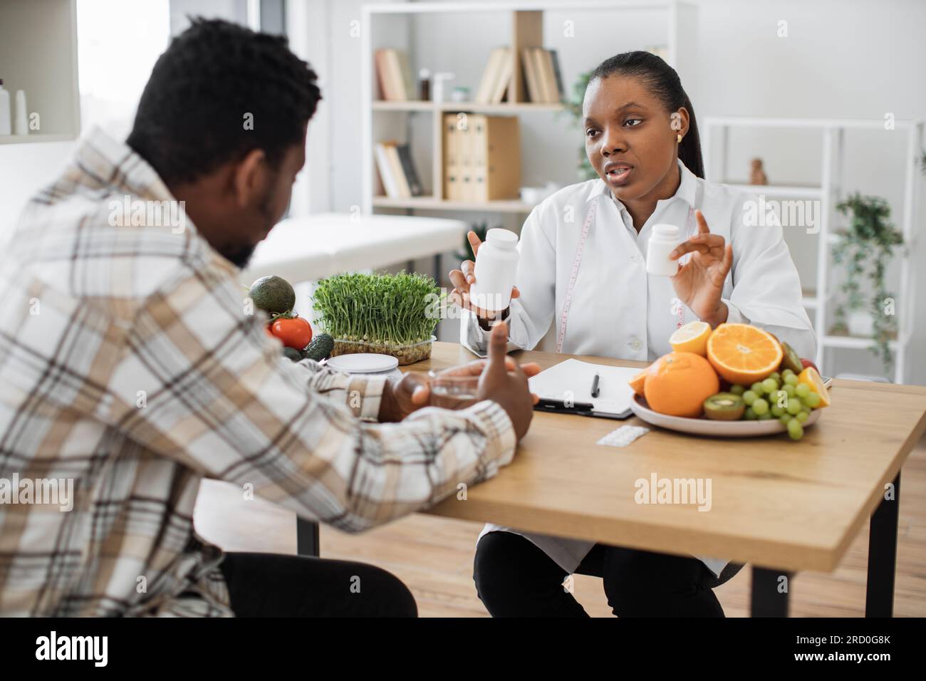Efficient female dietitian with bottle of pills in hand talking to ...