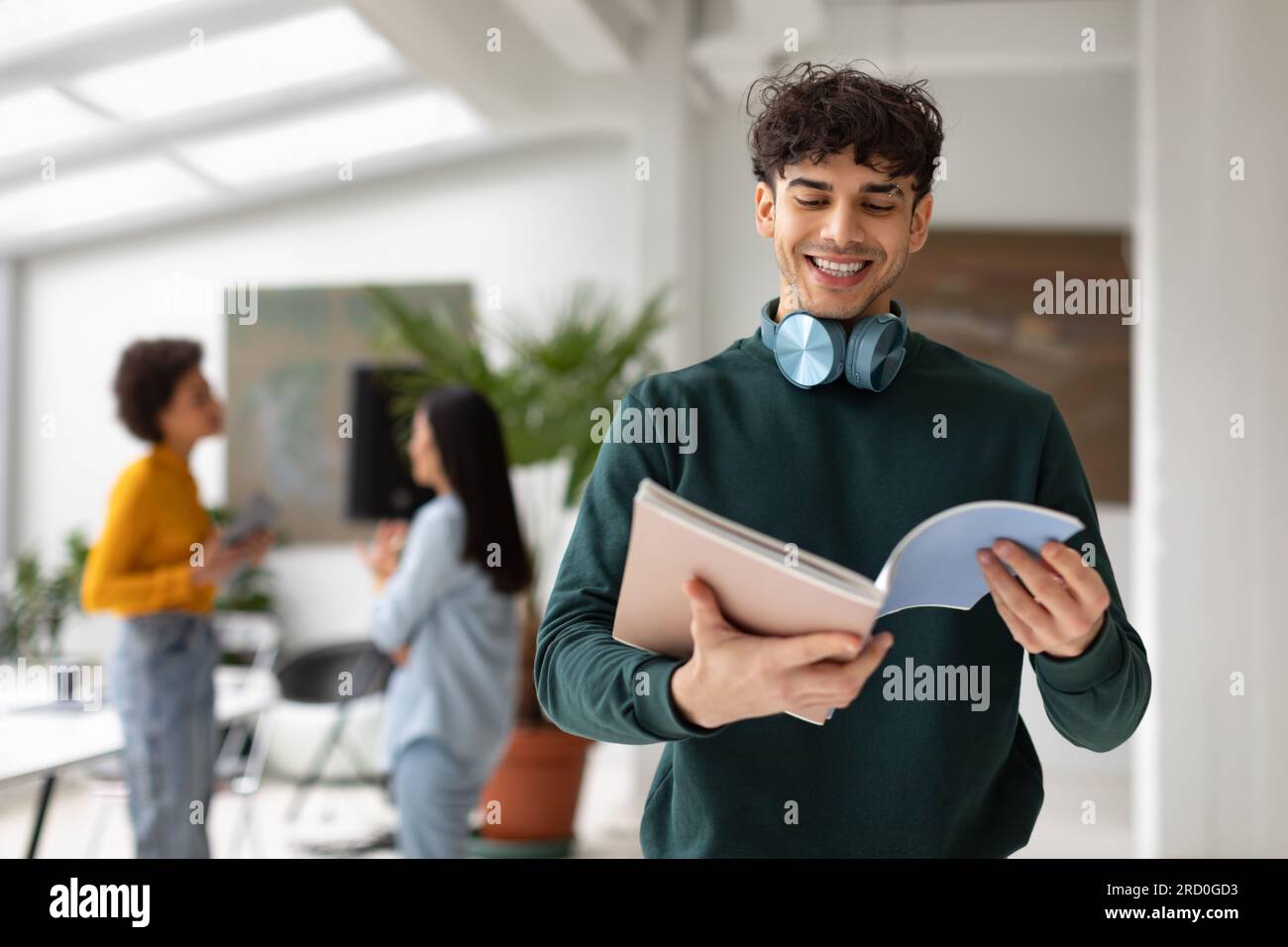 Positive male college student with headphones on neck holding open ...