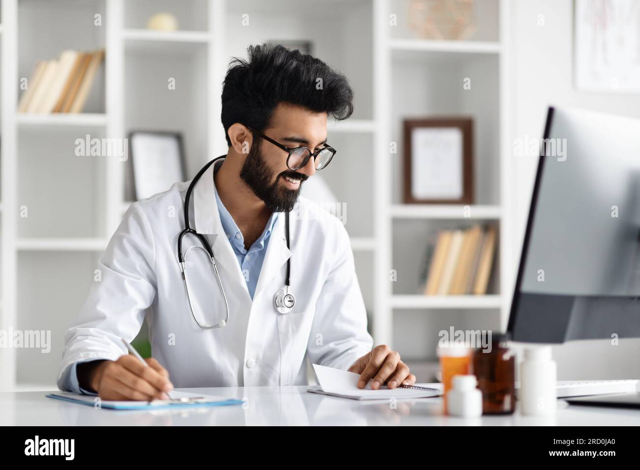 Handsome indian man doctor using computer and writing notes Stock Photo ...