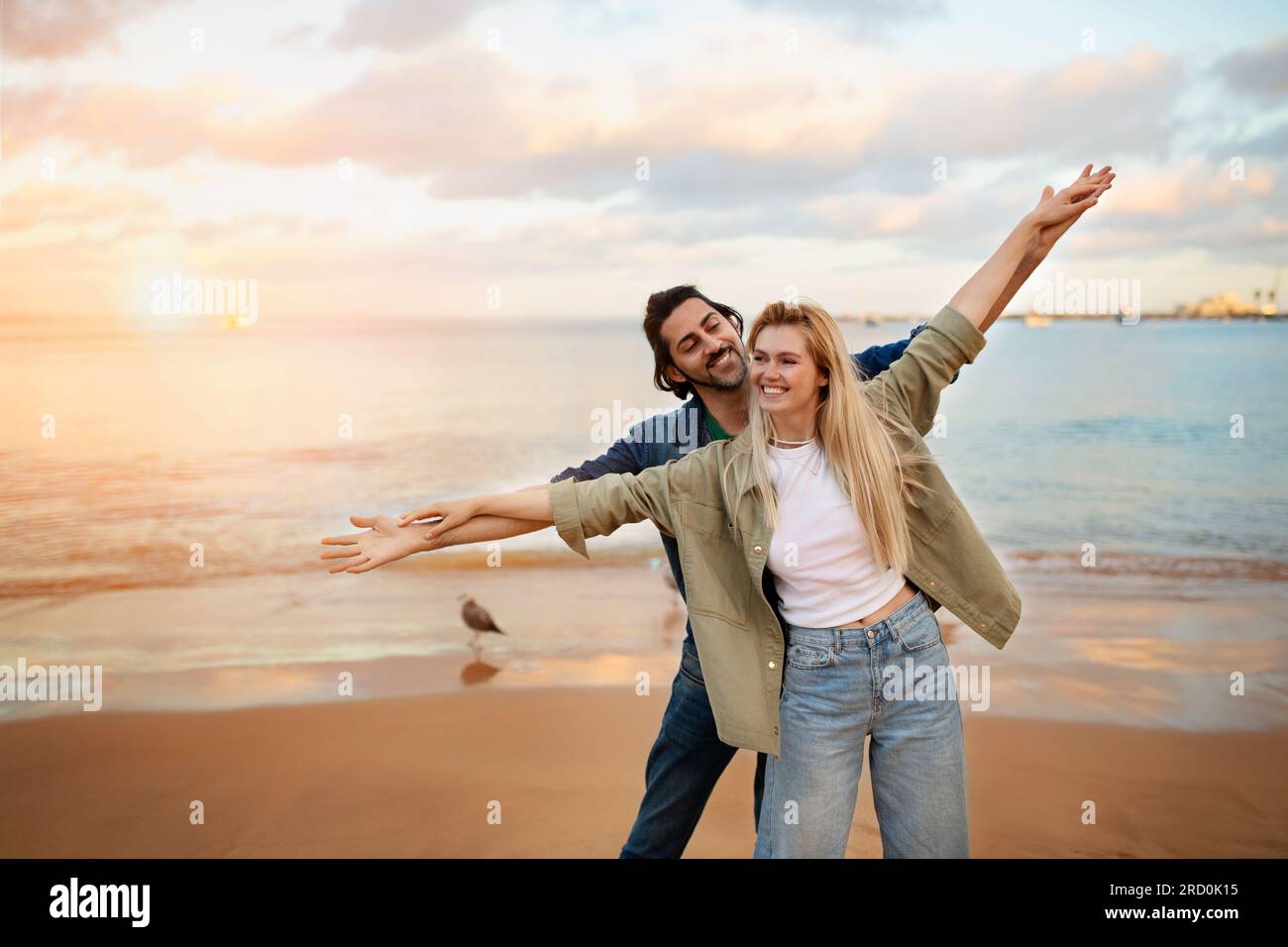 Young couple on beach pretending flying, spreading hands like wings ...