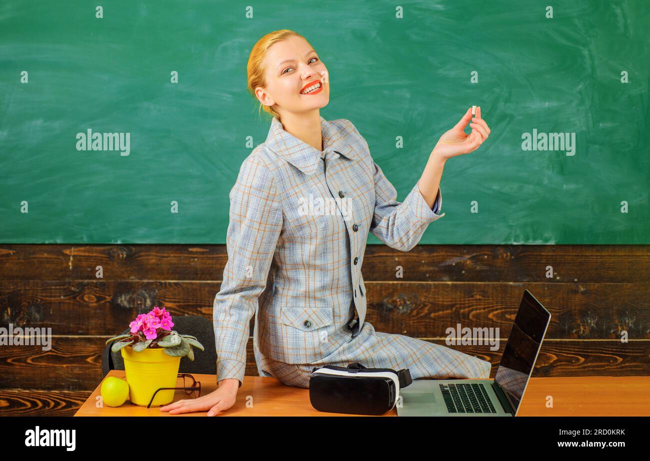 Smiling female teacher with chalk in front of chalkboard at classroom ...
