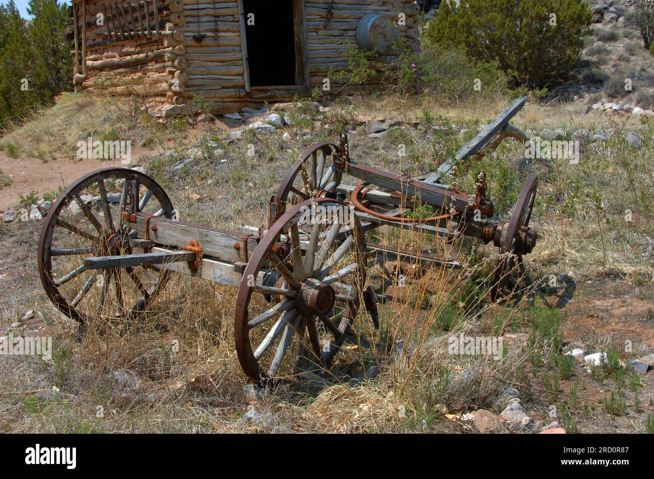 Old wagon sits in front of a rustic, log cabin. Steel wheels and wooden ...