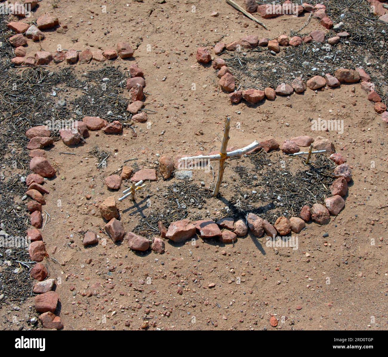 Tiny croses mark a tiny grave. Sticks form croses and red stones ...
