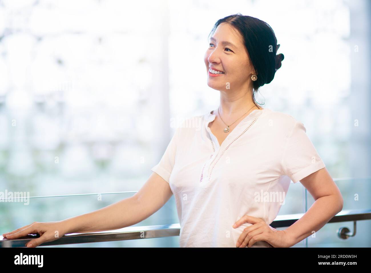 Asian woman indoors. Girl standing at big window in a modern office ...