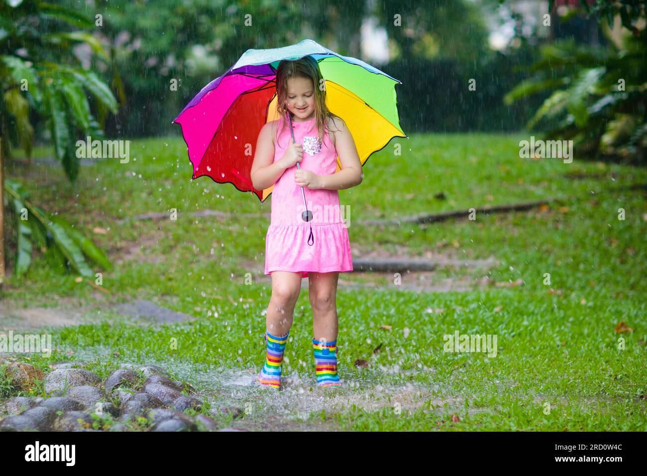 Kid playing out in the rain. Children with umbrella and rain boots play ...