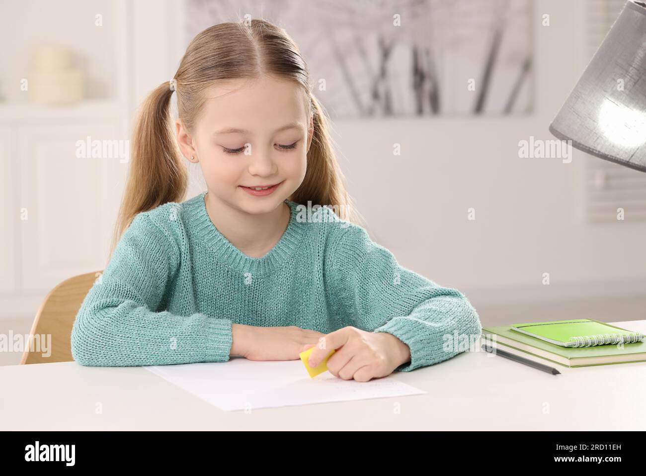 Girl using eraser at white desk in room Stock Photo - Alamy