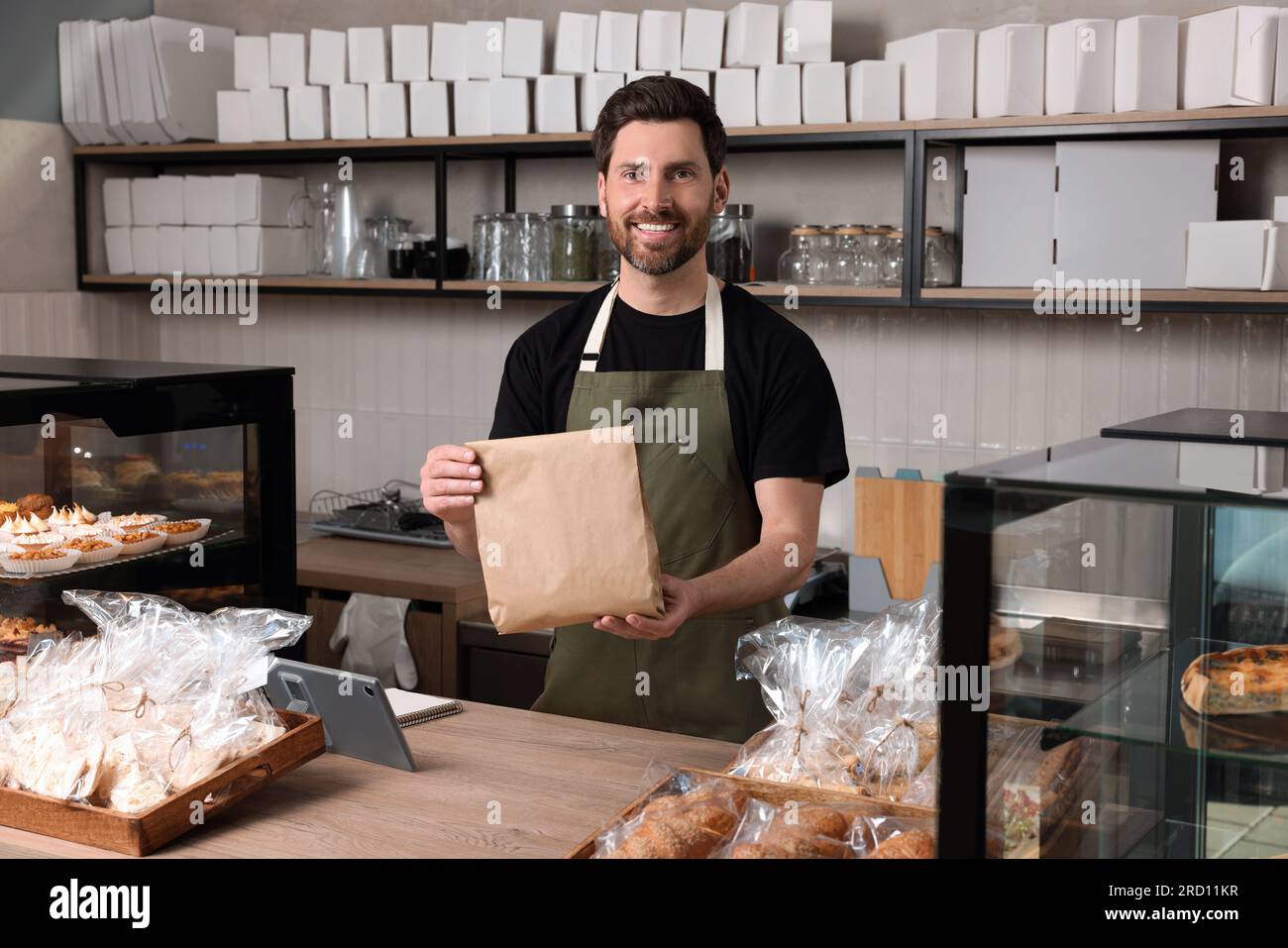 Happy seller with paper bag at cashier desk in bakery shop Stock Photo ...