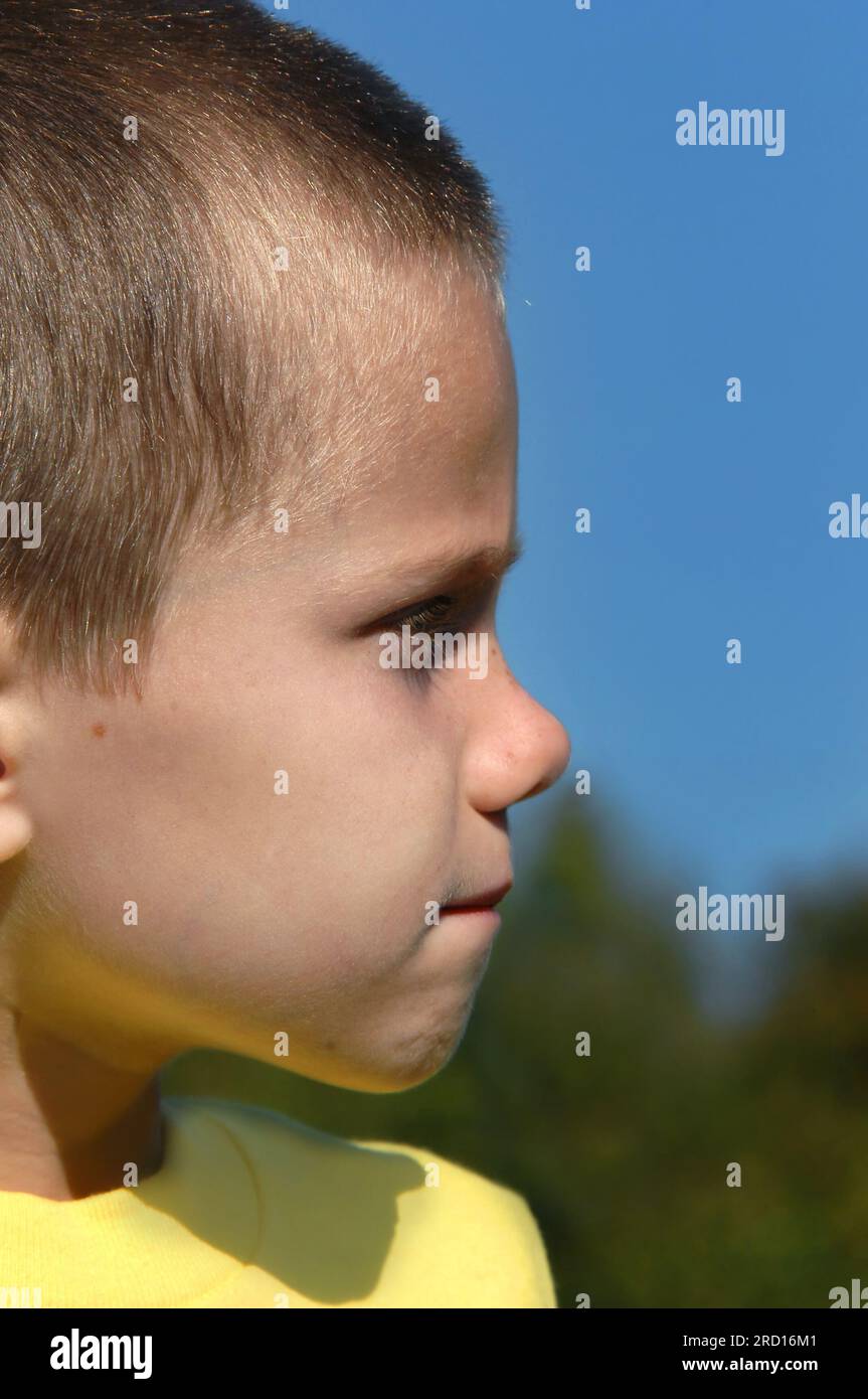 Little boy stars solemnly ahead, unsmiling, with his lips pursed. He is ...