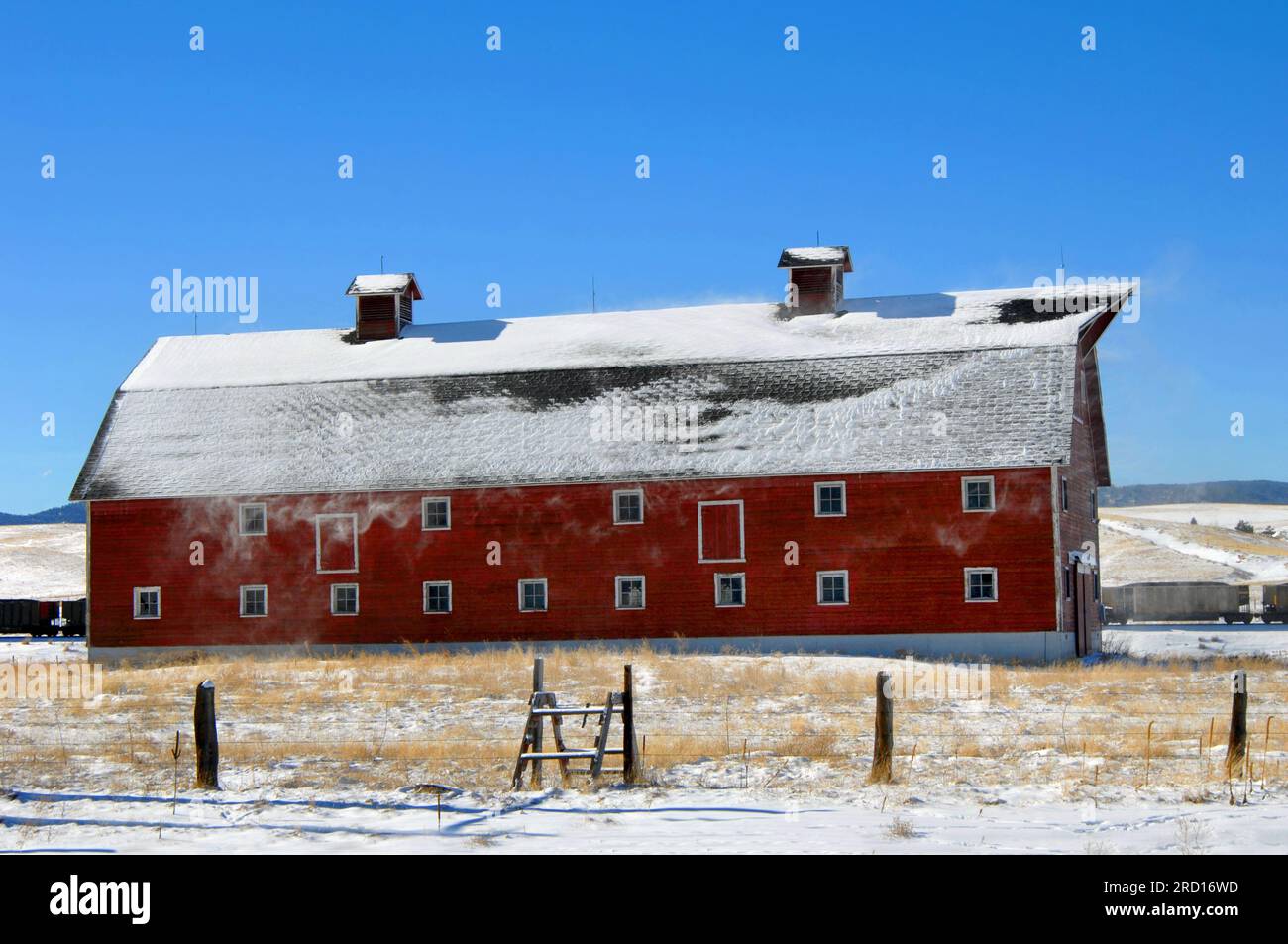 Snow blows from the rood of a red, wooden barn in a field in Colorado ...
