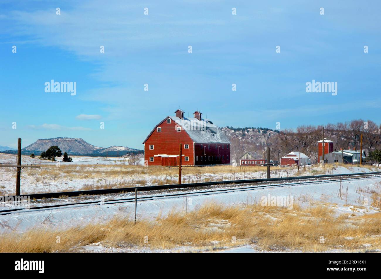 Snow lays around railroad tracks and sits on barn roof. Barn is a two ...