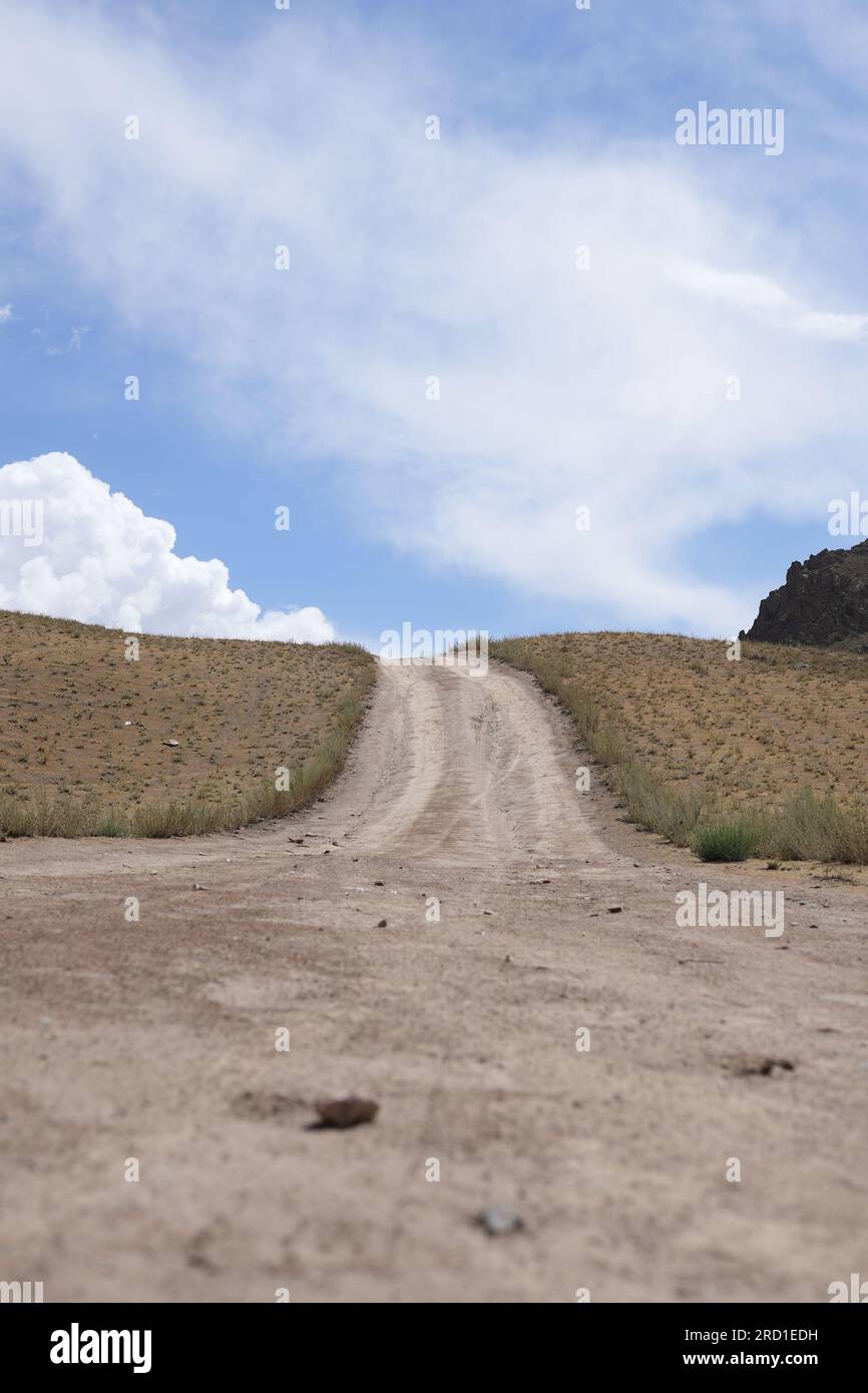 The cloudy blue sky overlooking dusty path towards the mountains Stock ...