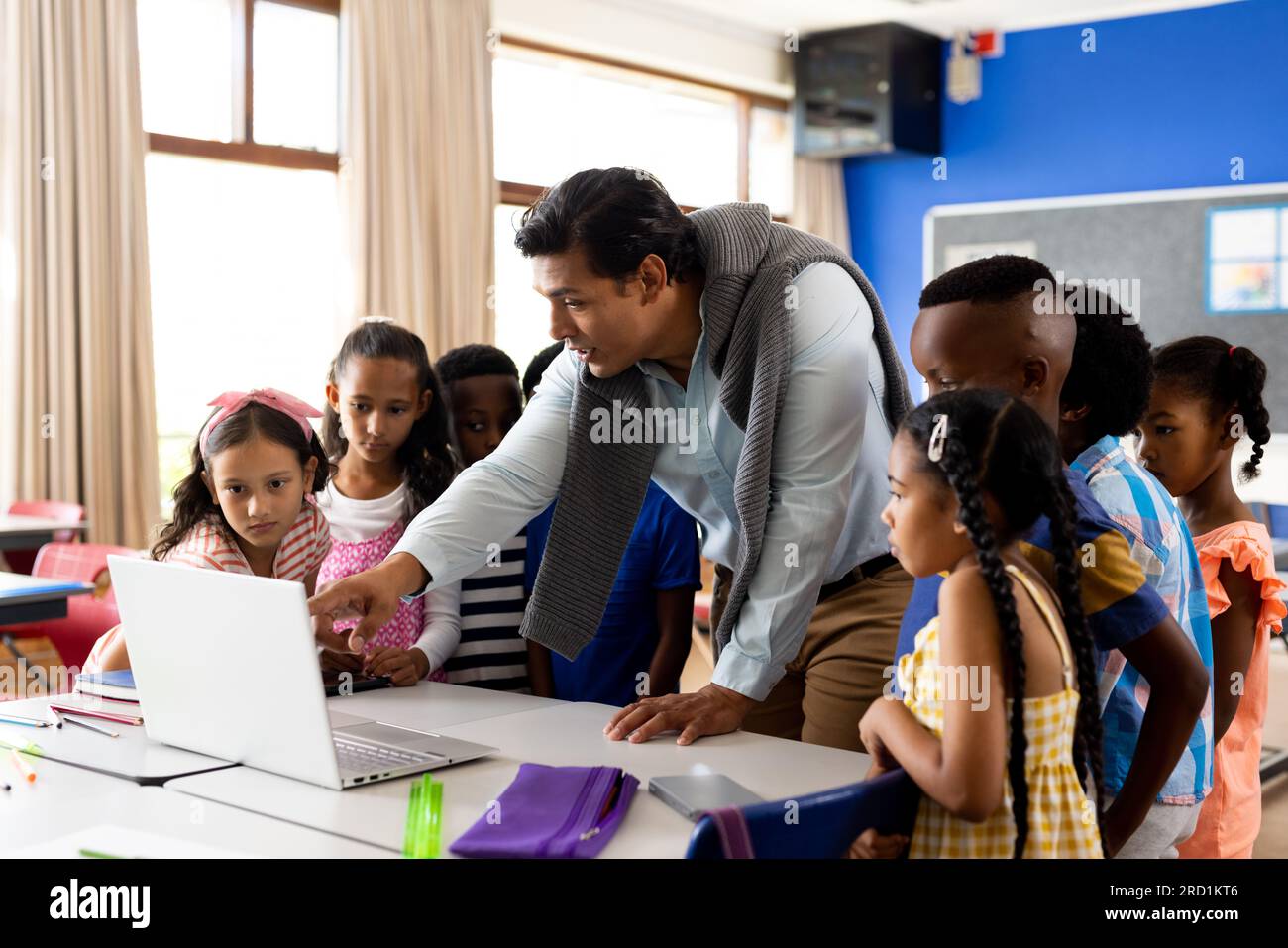 Diverse male teacher using laptop teaching children staying in ...